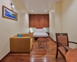 Quarto de hotel com cama, sofá, poltrona, mesa pequena e um quadro na parede.