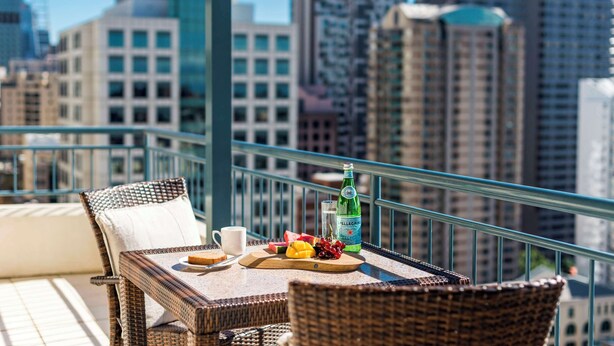 Uma varanda com mobiliário de vime, uma mesa com comida e bebidas, e vista para a cidade.