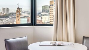 Quarto de canto com uma grande janela, uma mesa redonda e duas cadeiras.