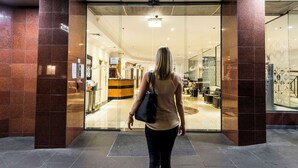 Mulher caminhando por um saguão de hotel, com uma recepção visível ao fundo.