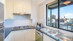 Uma cozinha moderna com armários brancos, fogão a gás, lava-louças e uma janela grande com vista para a cidade.