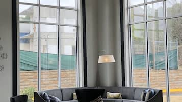 Uma sala de estar moderna com grandes janelas, um sofá preto, um abajur de chão e um lustre.
