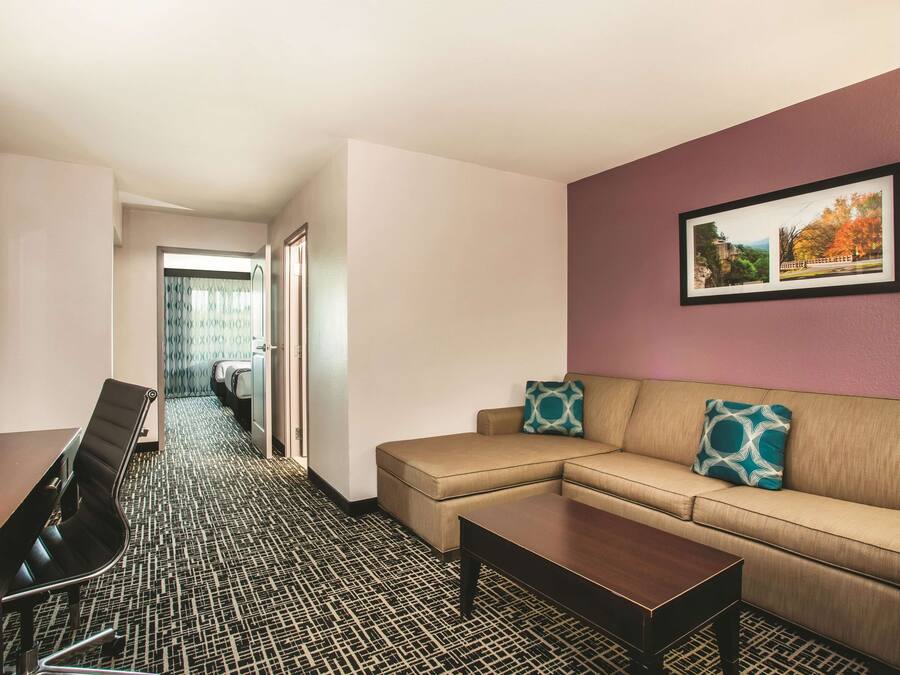 Quarto de hotel com sofá, mesa de centro, mesa de jantar e cadeiras, e carpete estampado.