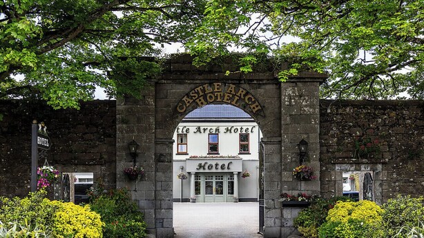 Entrada do Castelo Arch Hotel, com um arco de pedra, fachada branca e um letreiro sobre a entrada.