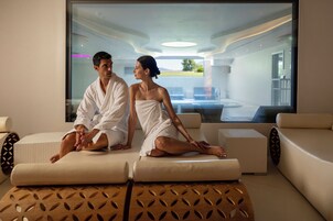 Um casal sentado em uma mesa de massagem em um spa, com vista para uma piscina e área externa.