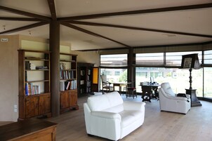 Uma sala de estar espaçosa com um sofá de couro branco, estantes de madeira e um espaço de jantar com mesa e cadeiras.