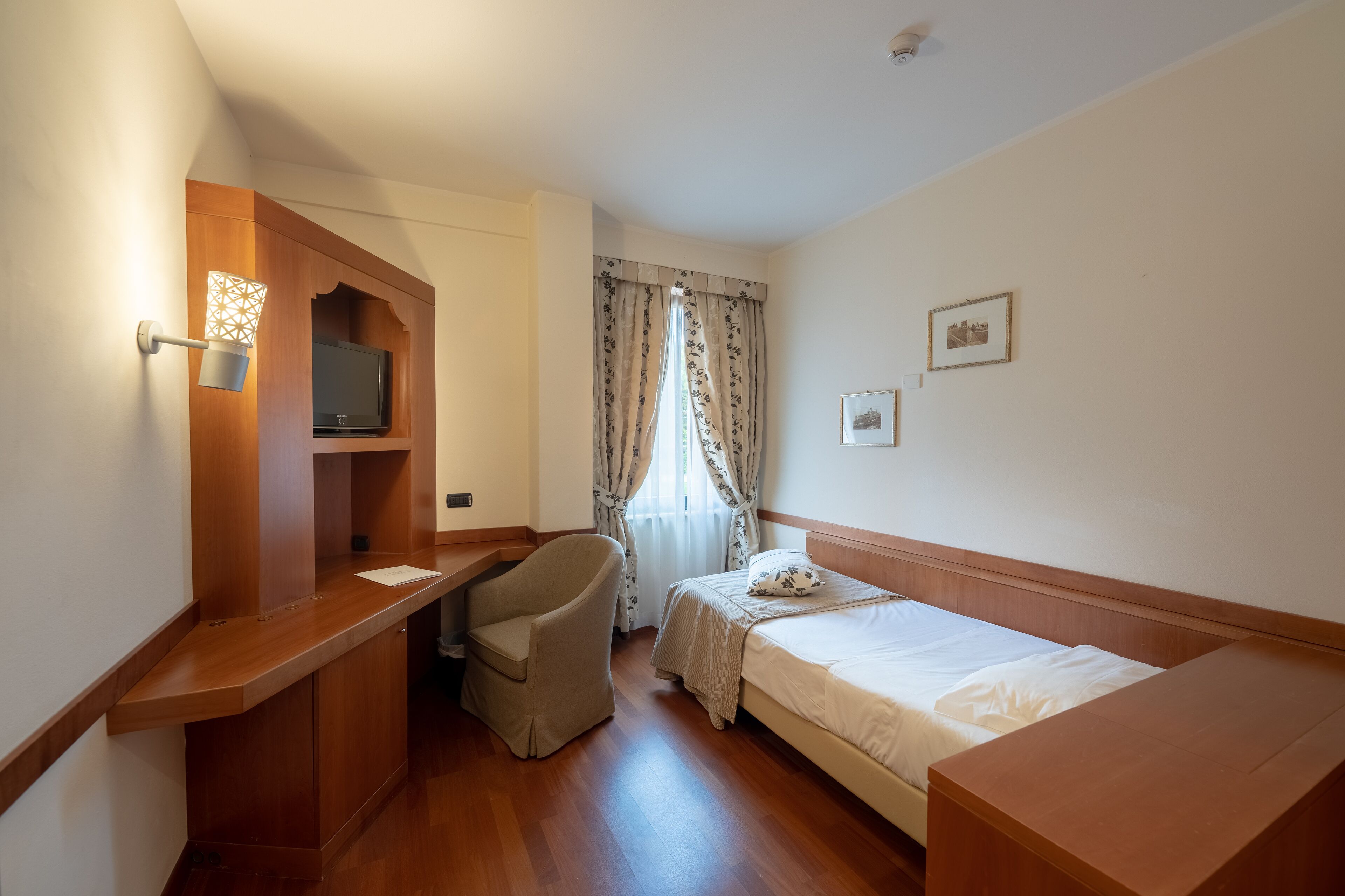 Quarto de hotel com uma escrivaninha de madeira, uma cadeira, uma cama e uma televisão.