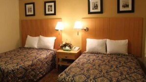 Quarto de hotel com duas camas, cada uma com colcha estampada, mesa de cabeceira com abajur e quadros nas paredes.