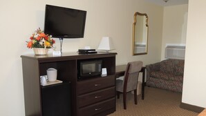 Quarto de hotel com televisão de tela plana, micro-ondas, escrivaninha com cadeira, cama, espelho e uma pequena lixeira.
