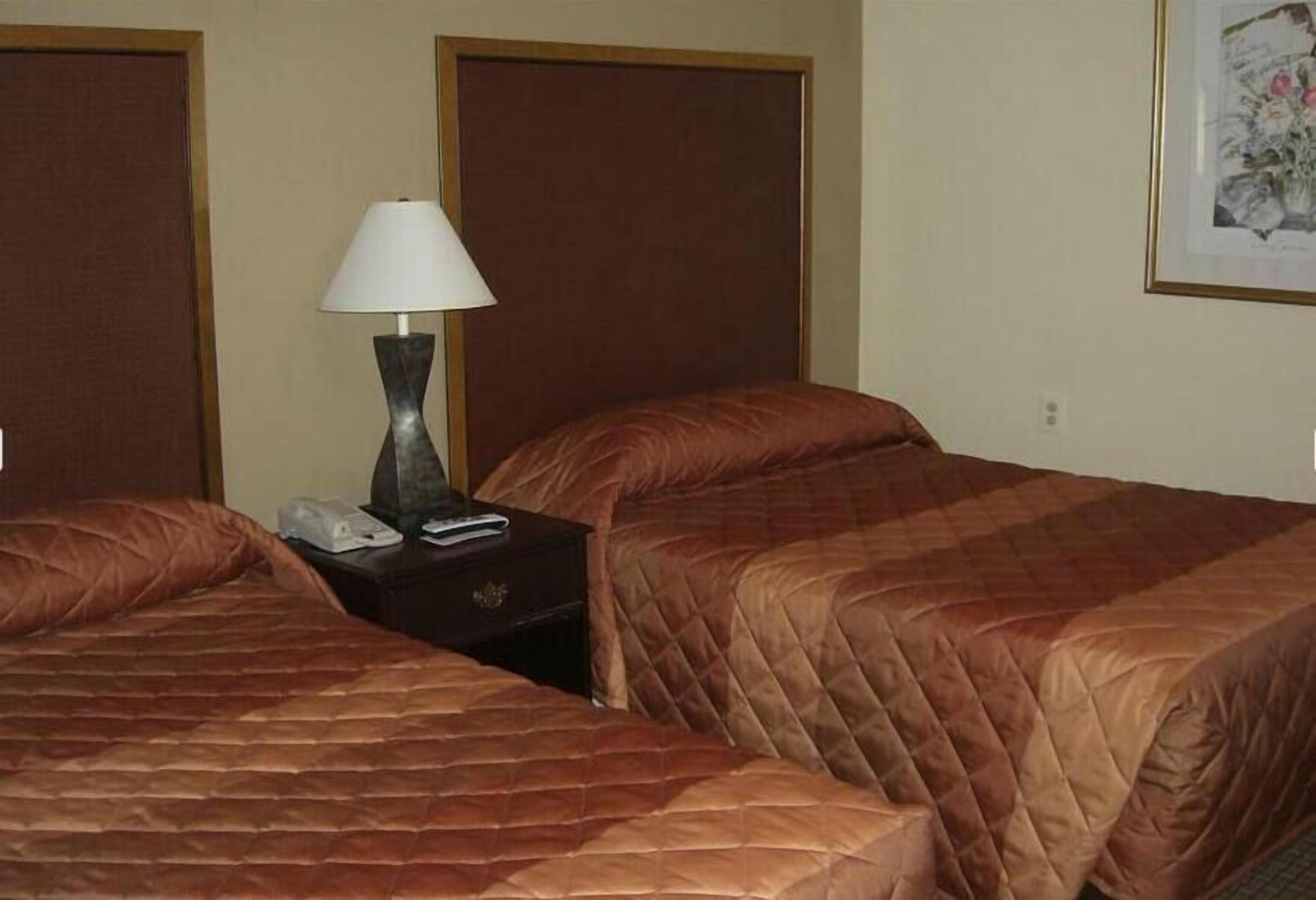 Quarto de hotel com duas camas, uma mesa de cabeceira com abajur e telefone.