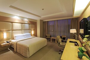 Quarto de hotel com uma cama grande, uma escrivaninha, uma cadeira, uma TV e um vaso com flores.