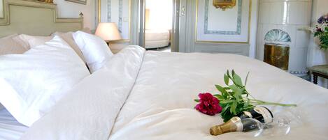 Quarto de hotel com uma cama grande, mesa de cabeceira com luminária, espelho e um vaso com flores.