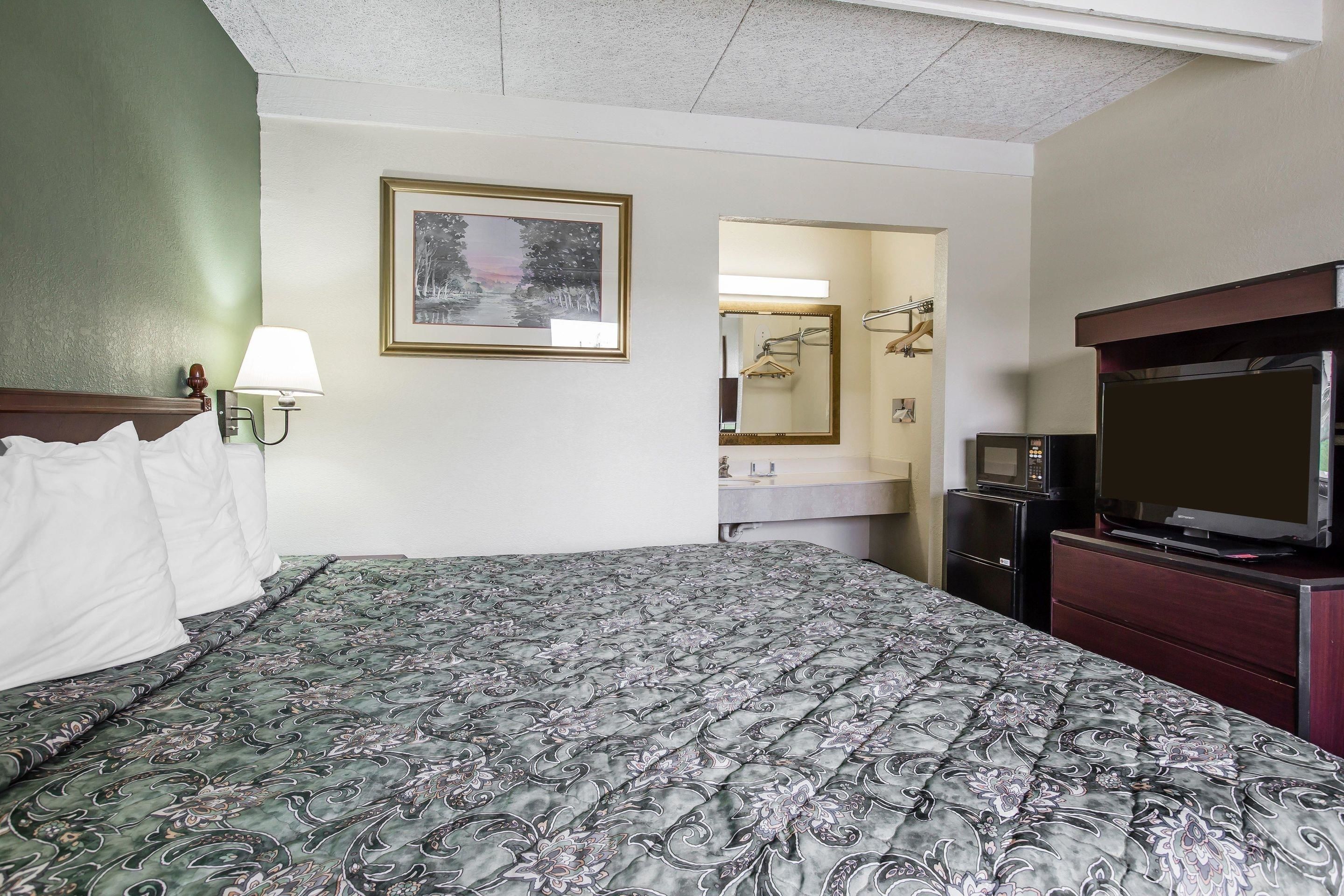Quarto de hotel com uma cama grande, penteadeira, televisão, espelho e um quadro na parede.