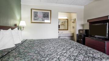 Quarto de hotel com uma cama grande, penteadeira, televisão, espelho e um quadro na parede.
