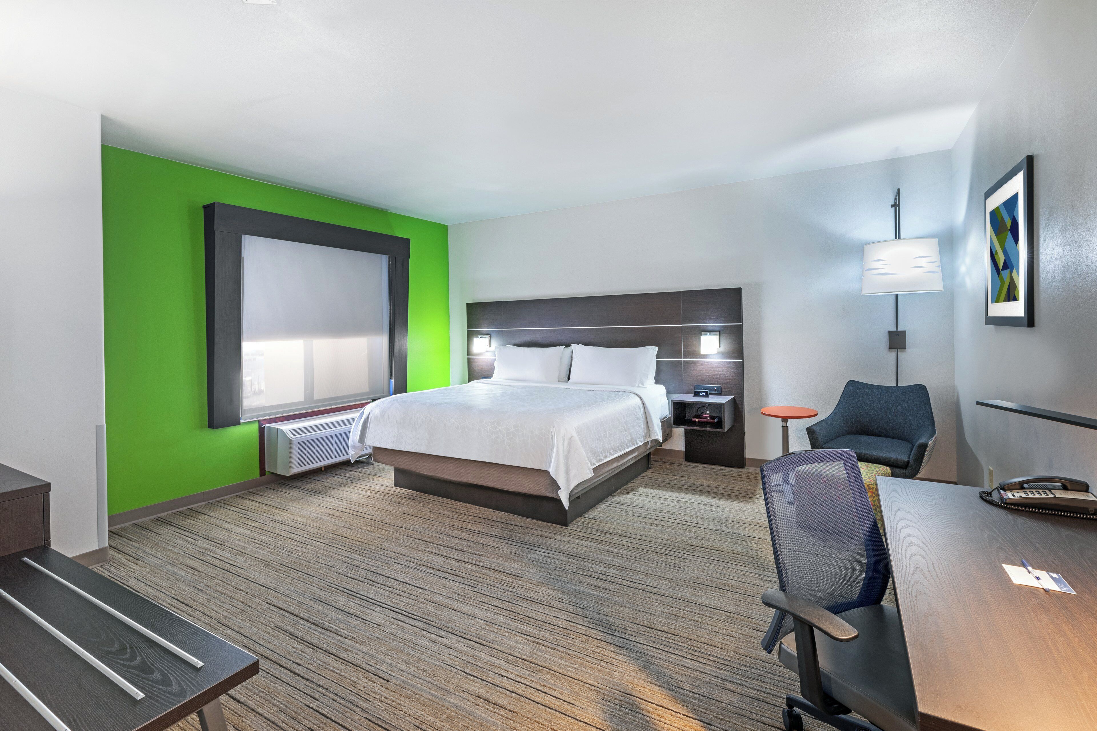 Quarto de hotel com cama, mesa de cabeceira, cadeira, escrivaninha e luminária.