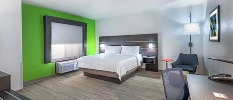 Quarto de hotel com cama, mesa de cabeceira, cadeira, escrivaninha e luminária.