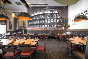 Interior de restaurante com várias mesas e cabines, um grande mural em estilo Coliseu na parede e luminárias pendentes.