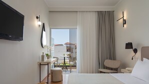 Quarto de hotel com cama, escrivaninha com cadeira, TV fixada na parede e vista para a varanda.