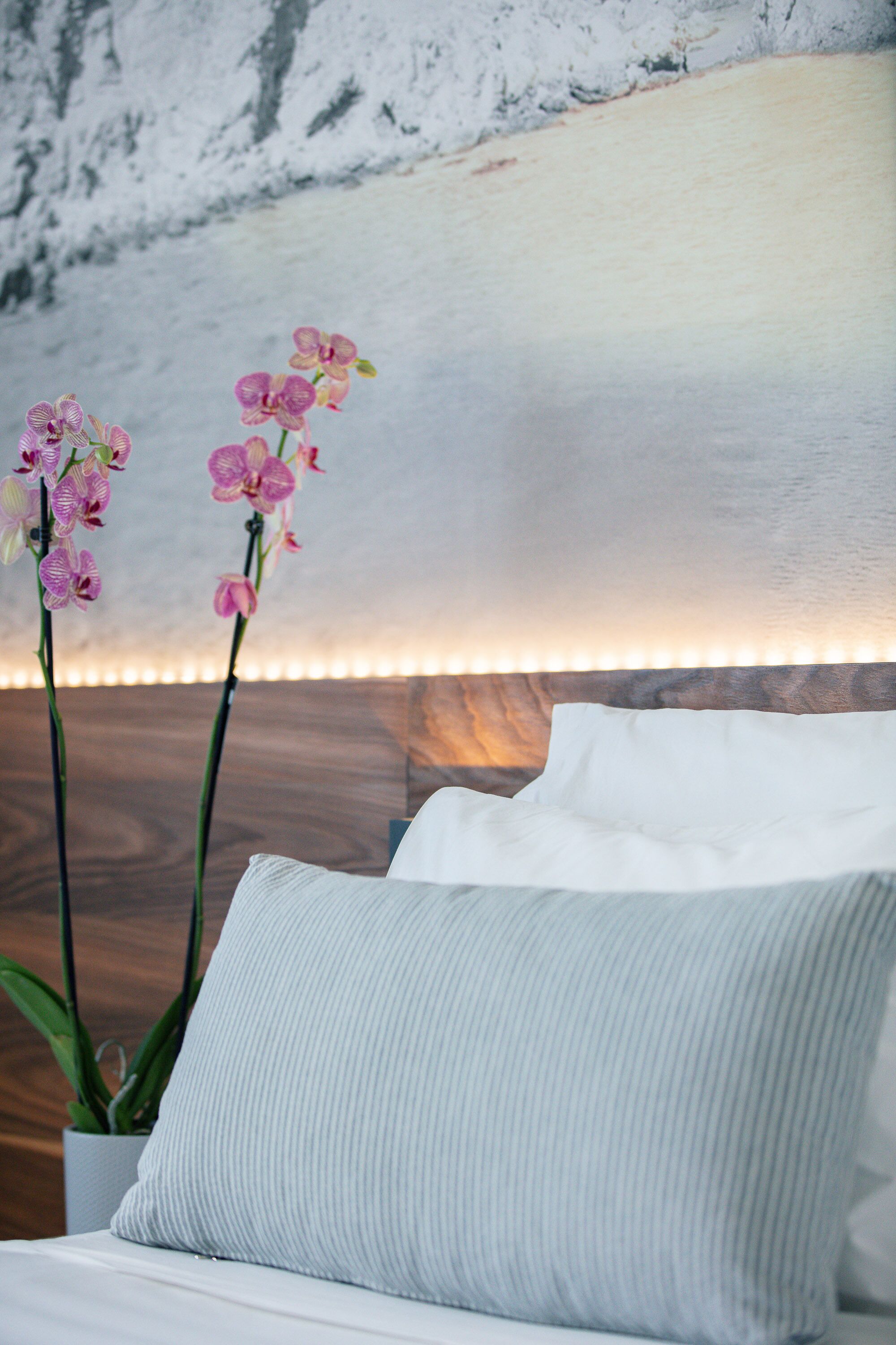 Quarto com cama, almofadas brancas e orquídeas rosa.