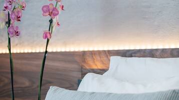 Quarto com cama, almofadas brancas e orquídeas rosa.