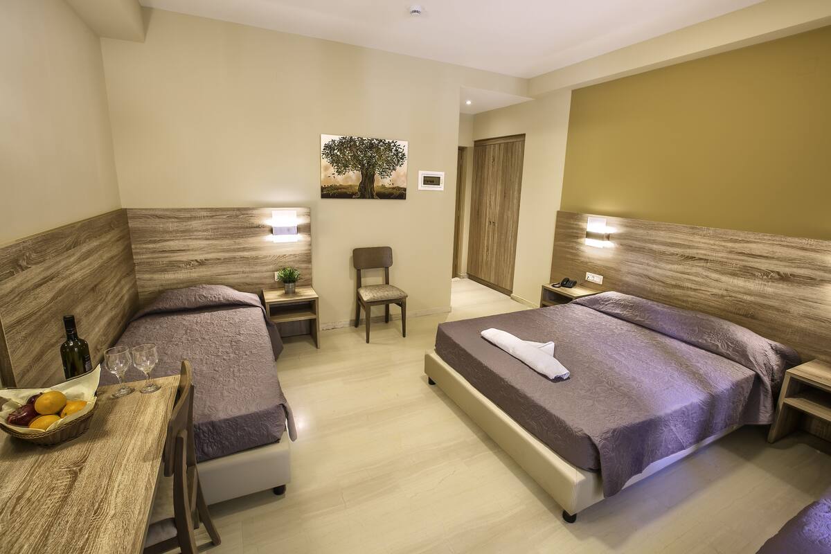Quarto de hotel com duas camas, uma mesa pequena com uma cesta de frutas, uma cadeira e uma mesa de cabeceira com abajur.