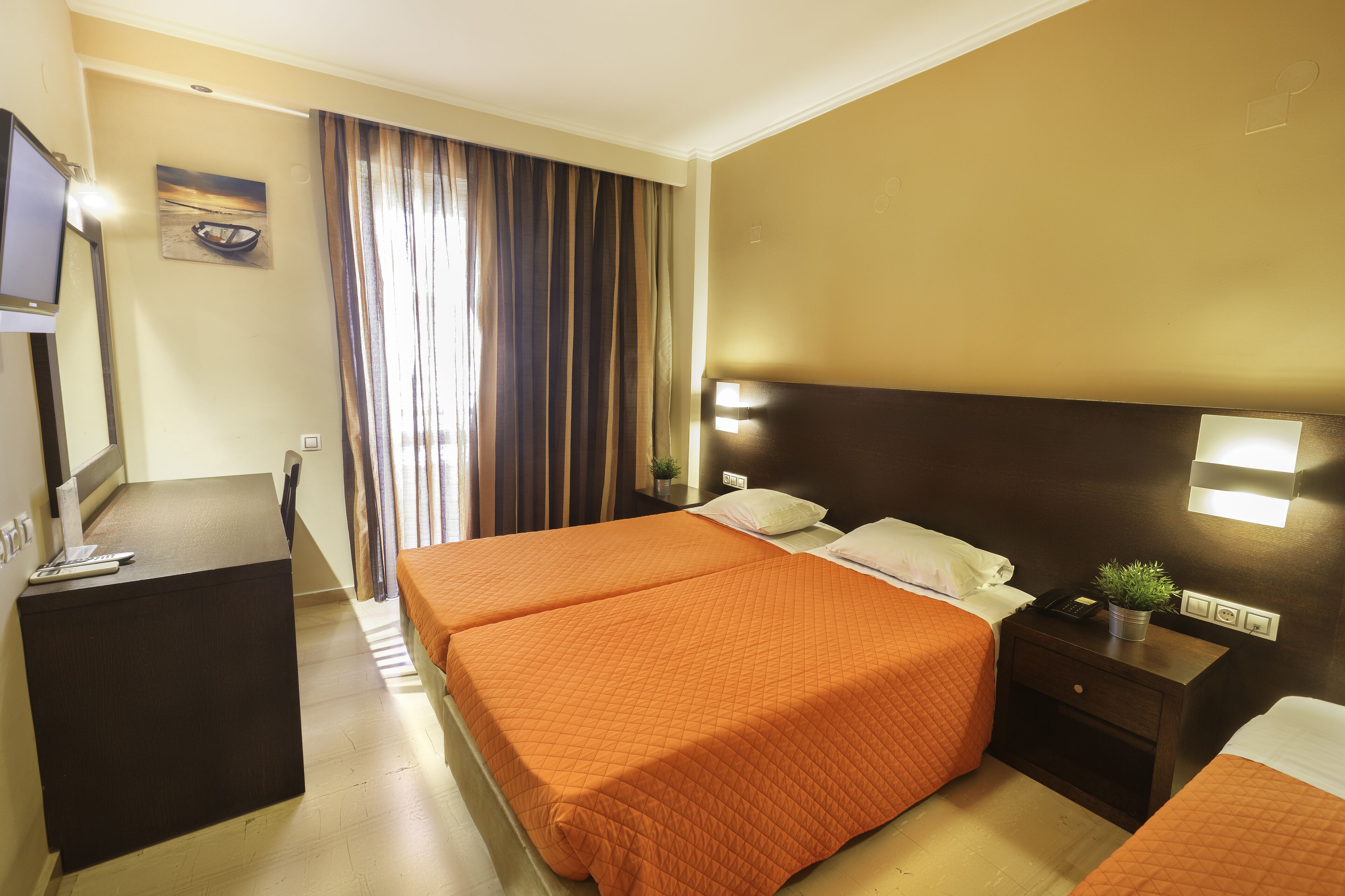 Quarto de hotel com duas camas, uma escrivaninha, televisão e mesa de cabeceira com abajur.