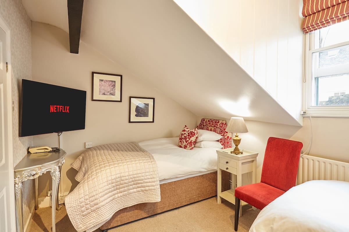 Quarto com cama, escrivaninha, cadeira, televisão e janela.