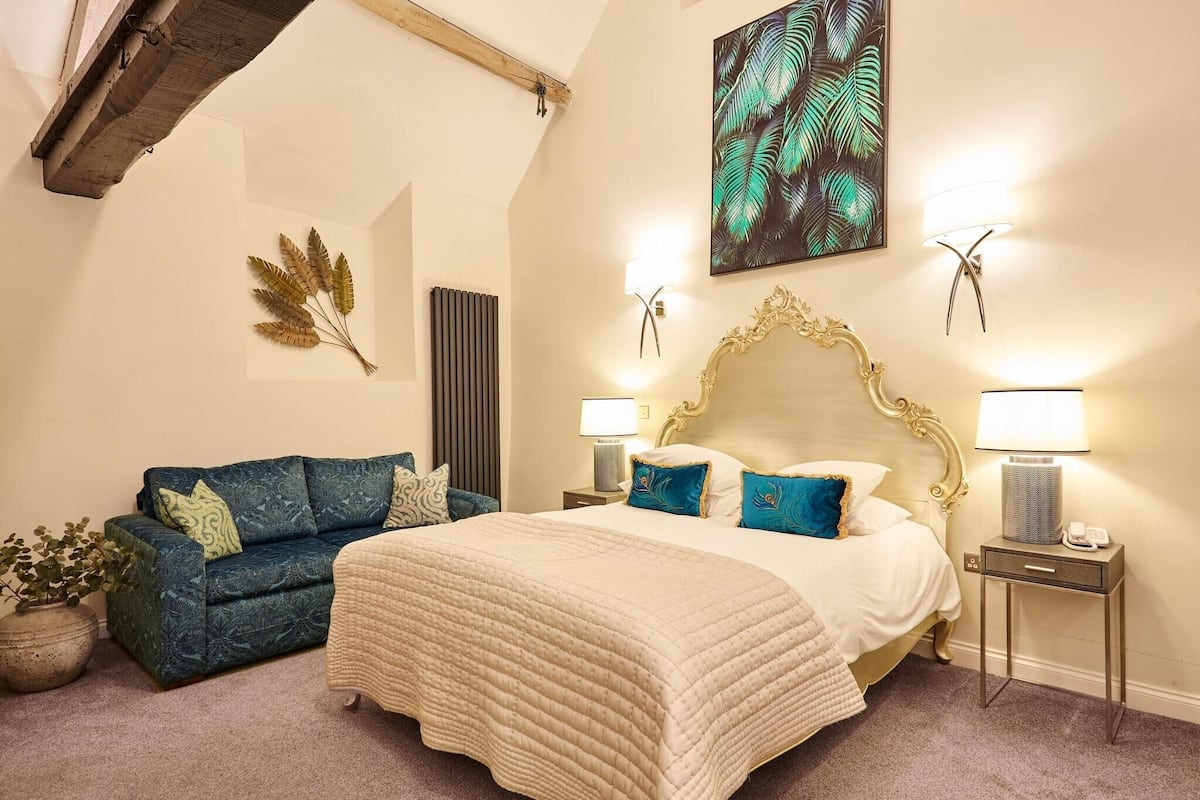 Quarto com cama, sofá azul, obras de arte decorativas e abajures.