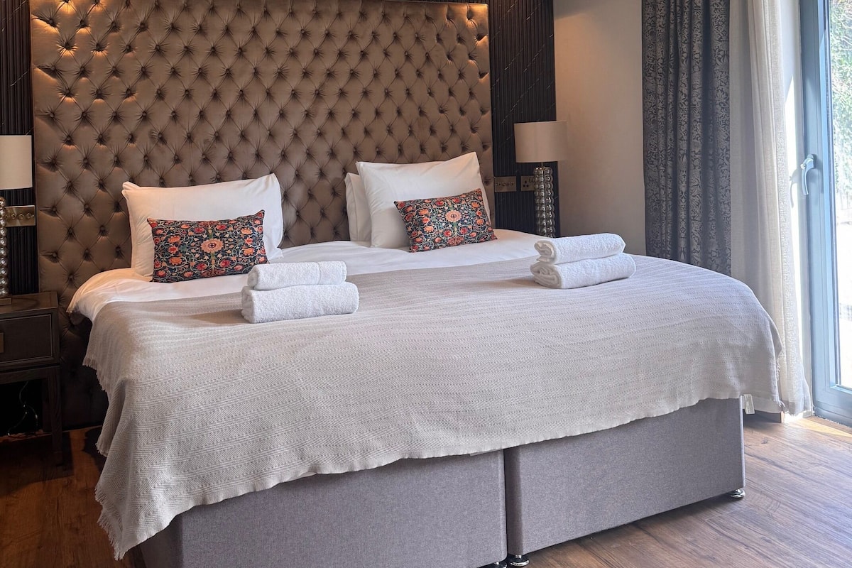 Uma cama grande com cabeceira estofada, duas almofadas e um lustre decorativo.