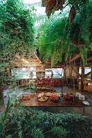 Um jardim interno com diversas plantas e uma mesa de madeira exibindo comida.