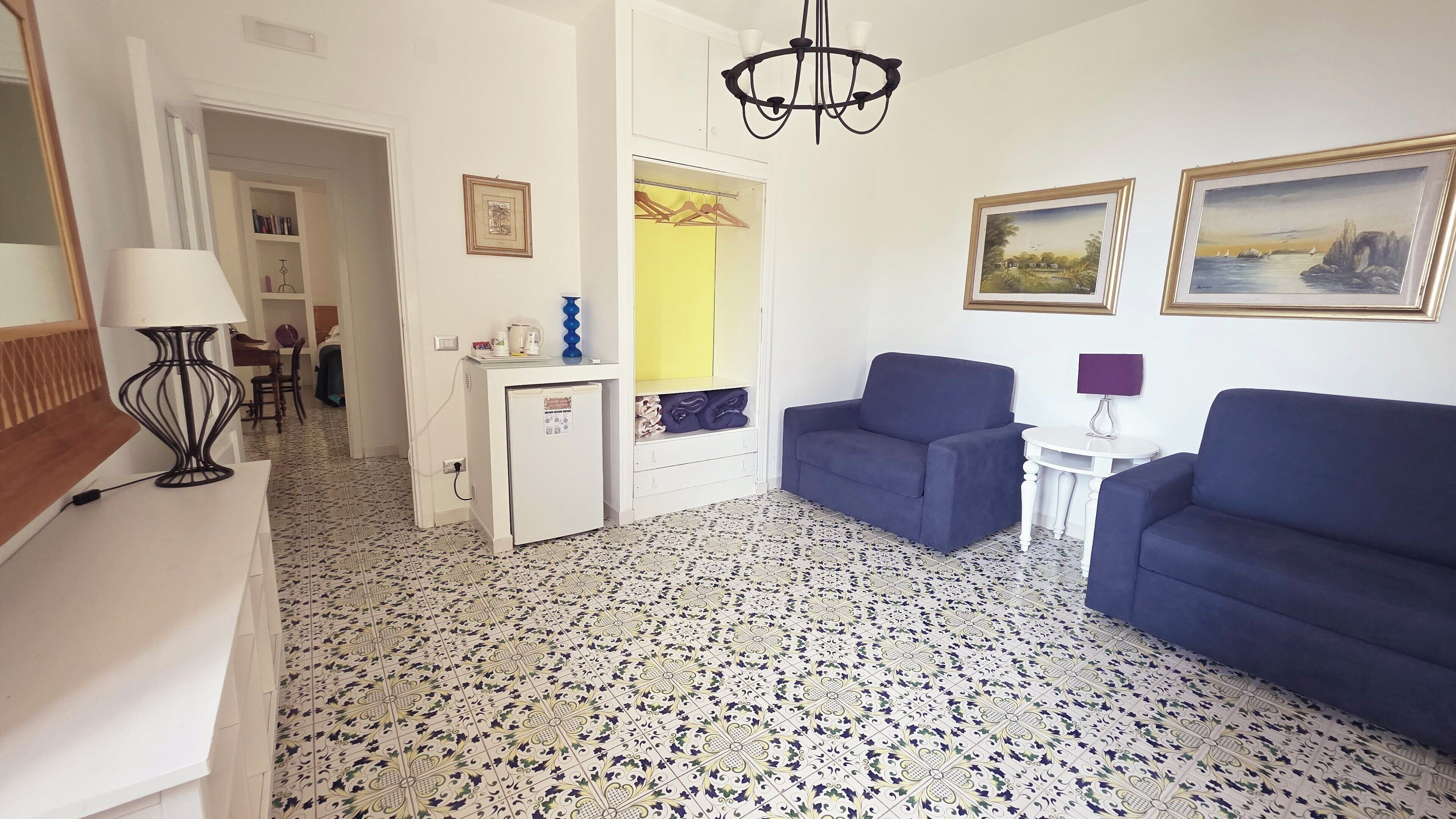 Sala de estar com piso estampado, geladeira, dois sofás, uma mesinha e um abajur.