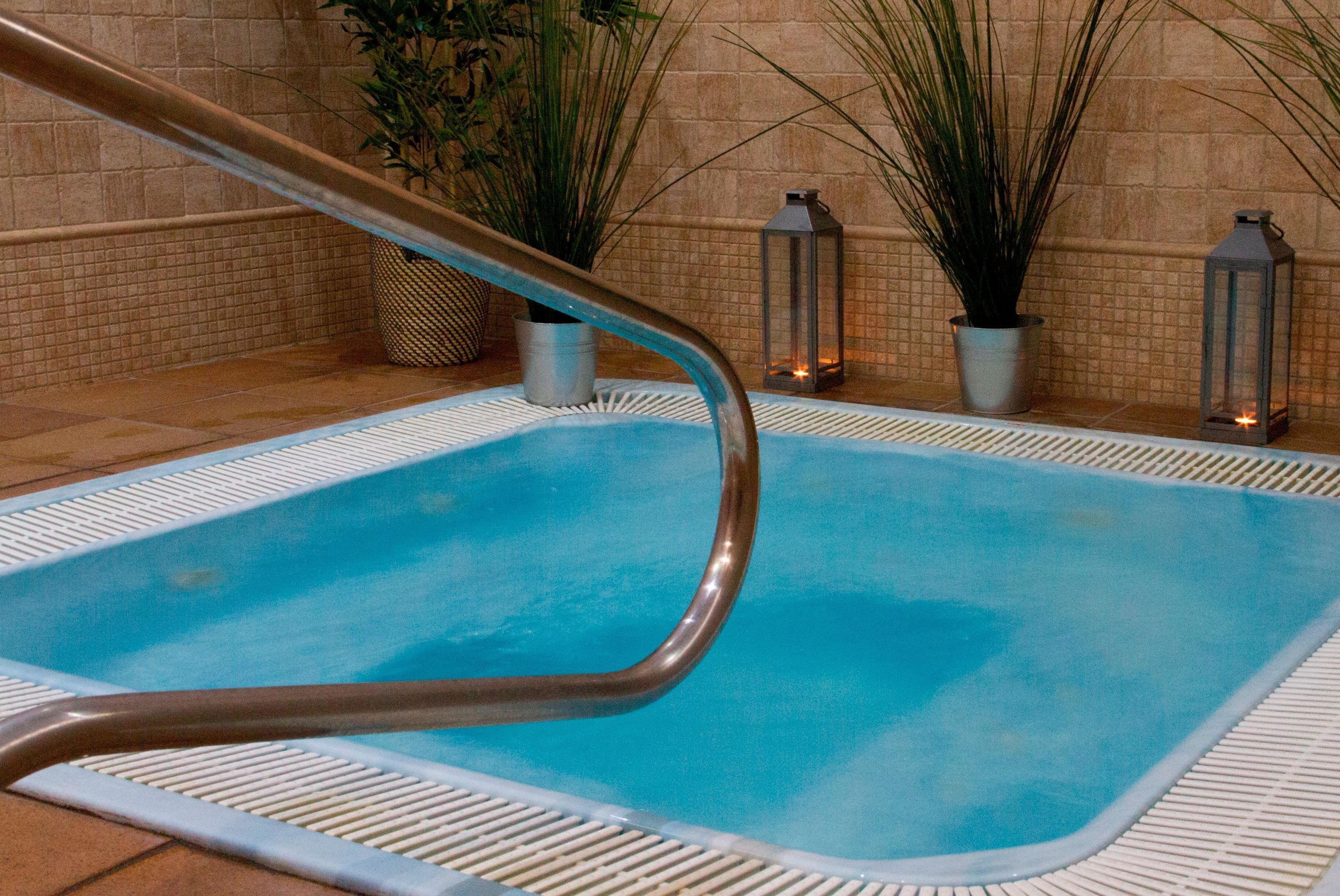 Piscina com escada de metal, rodeada por vasos de plantas e lanternas.