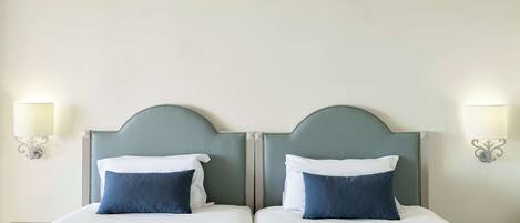 Uma cama de casal com duas almofadas, uma cabeceira e duas luminárias fixadas na parede.