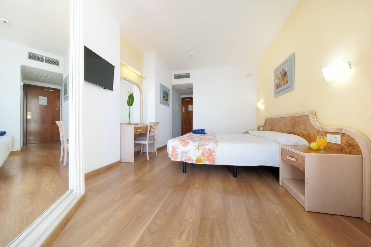 Quarto de hotel com cama, mesa de cabeceira, escrivaninha, cadeira e espelho.