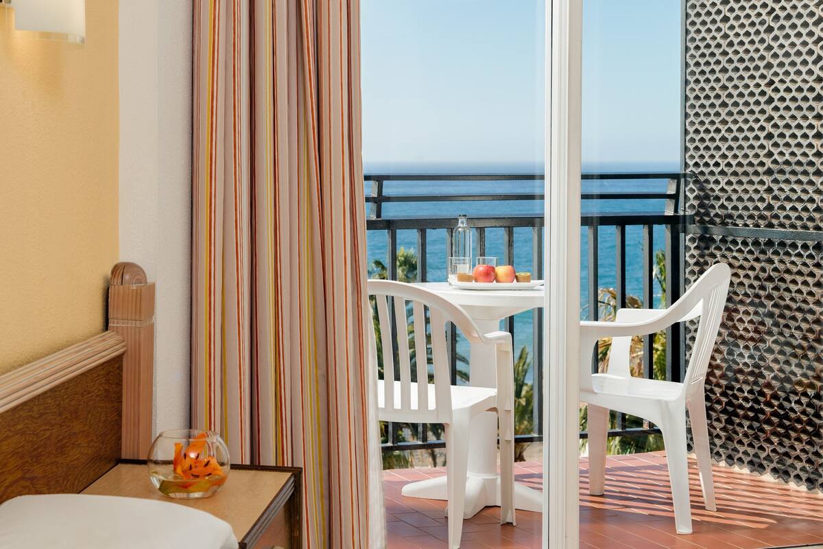 Varanda com mesa e cadeiras, vista para o mar e cortina decorativa.