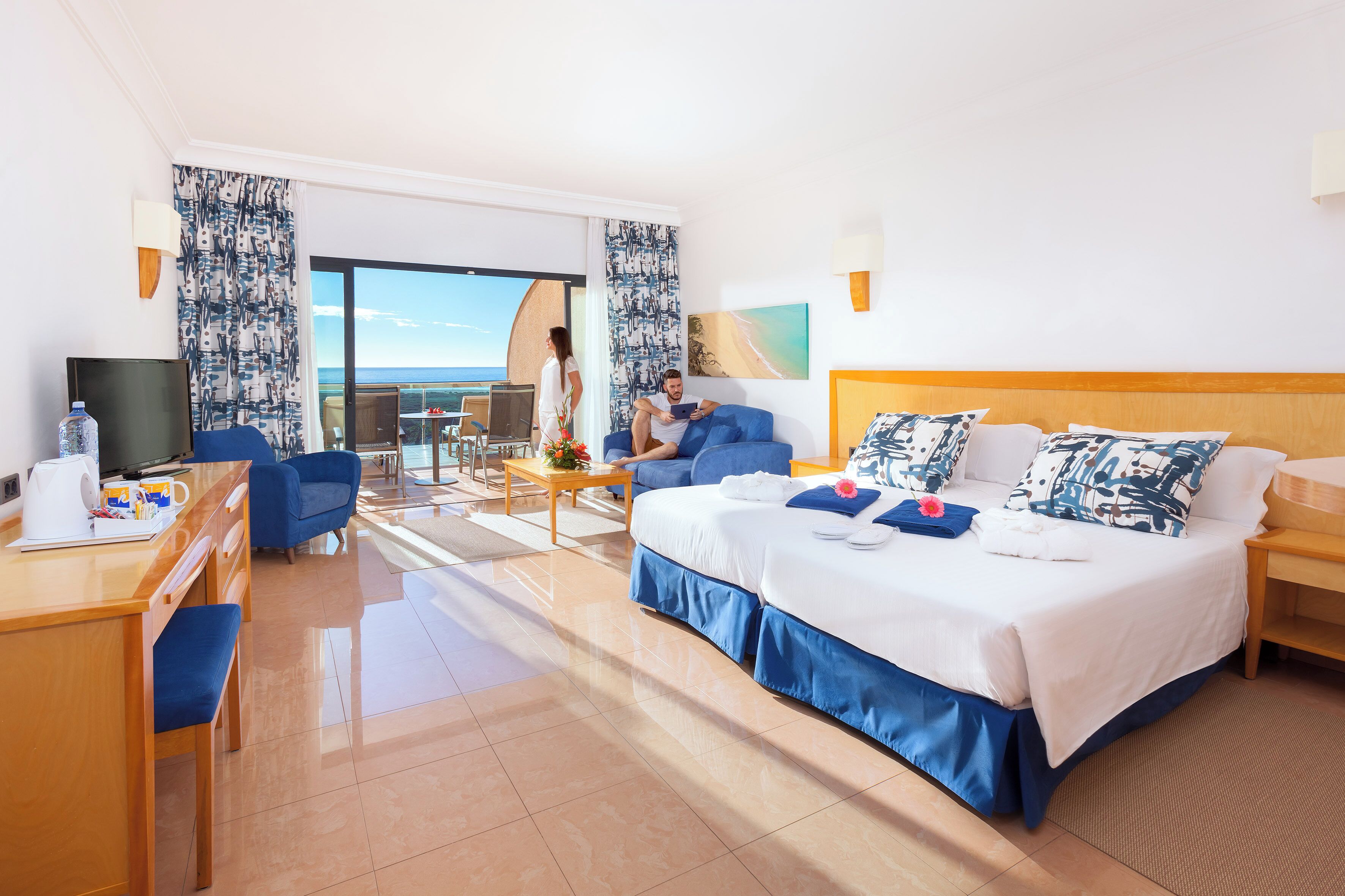 Quarto de hotel com cama, escrivaninha, cadeira, televisão e varanda com vista.
