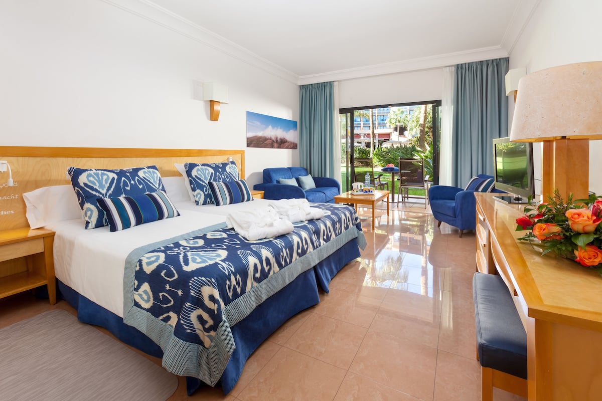 Quarto de hotel com cama, sofá, escrivaninha e televisão.