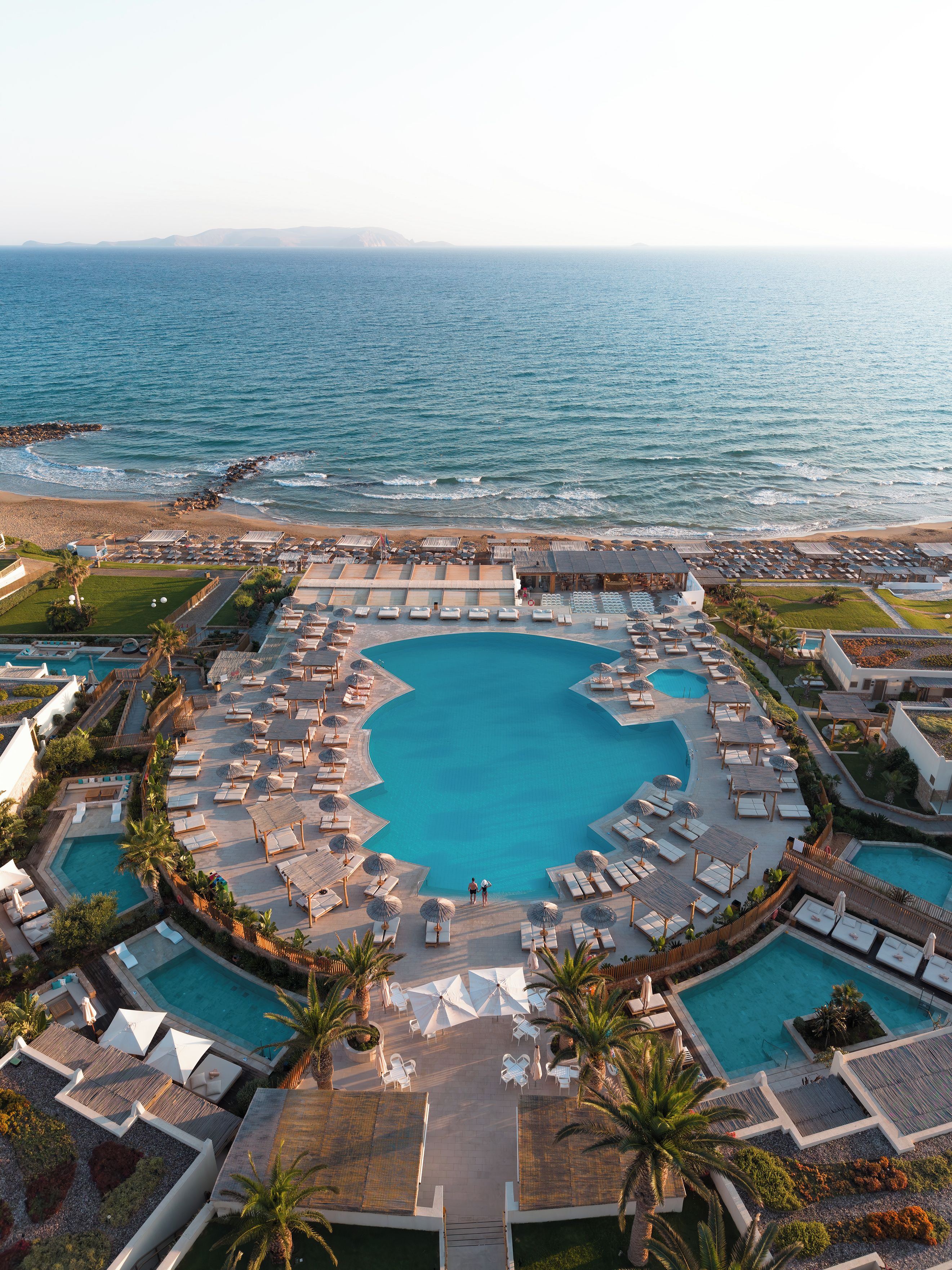 Resort com piscina central cercada por áreas de descanso e uma praia.