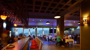 Um restaurante com um balcão comprido, assentos acolchoados vermelhos, copos de vinho pendurados e vista para as montanhas.