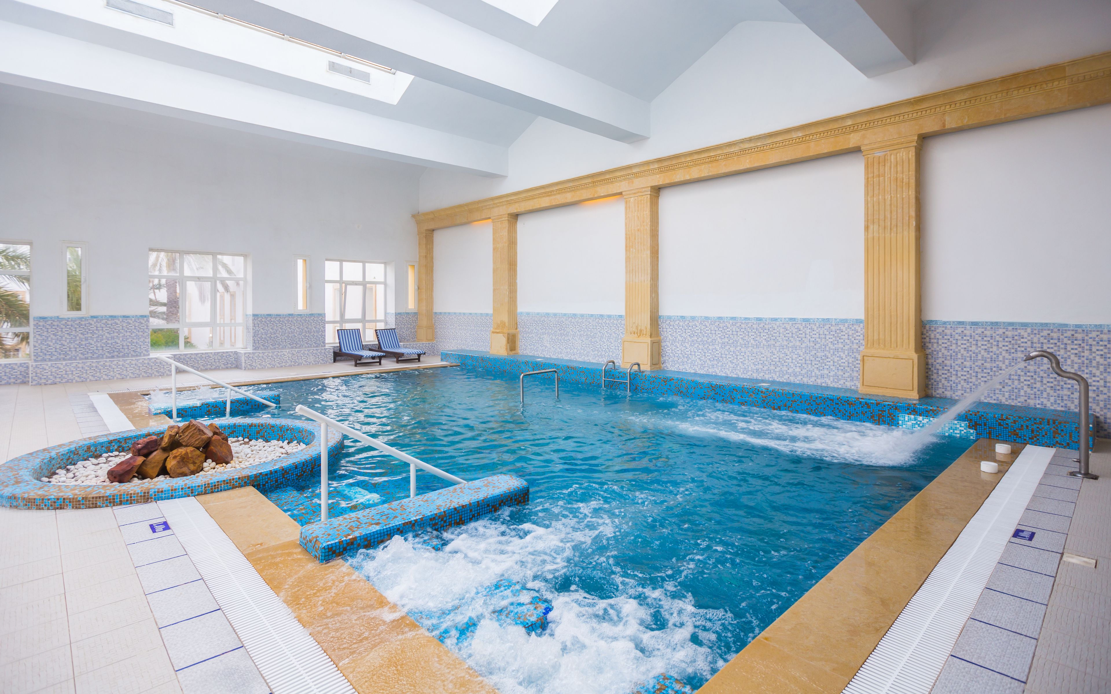 Piscina interior com área de hidromassagem, espreguiçadeiras e piso ladrilhado.