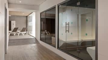 Corredor moderno de hotel com área de spa com paredes de vidro, balcão de recepção e área de estar com cadeiras.