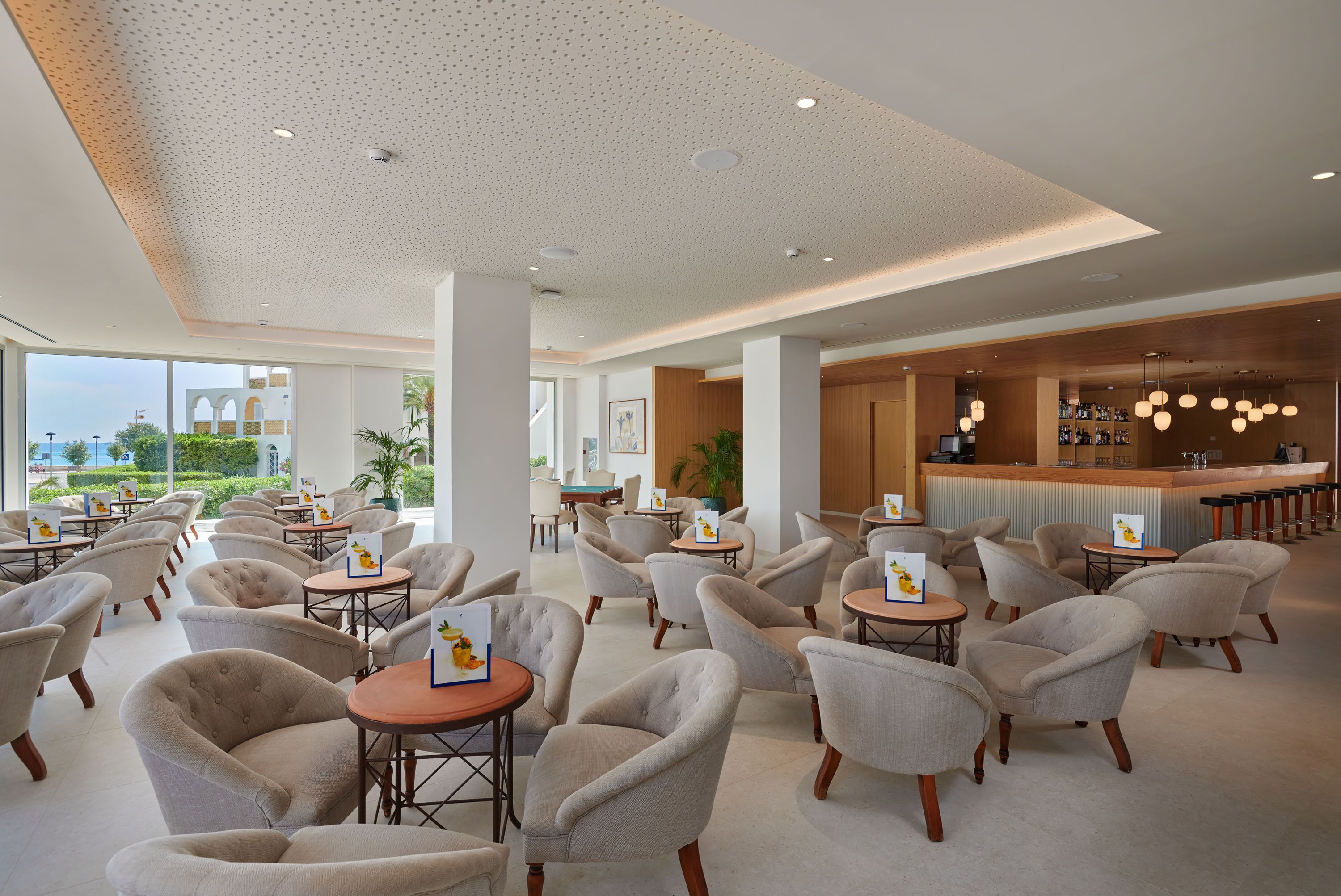 Um lobby de hotel moderno com assentos confortáveis, área de bar e janelas amplas com vista para o exterior.