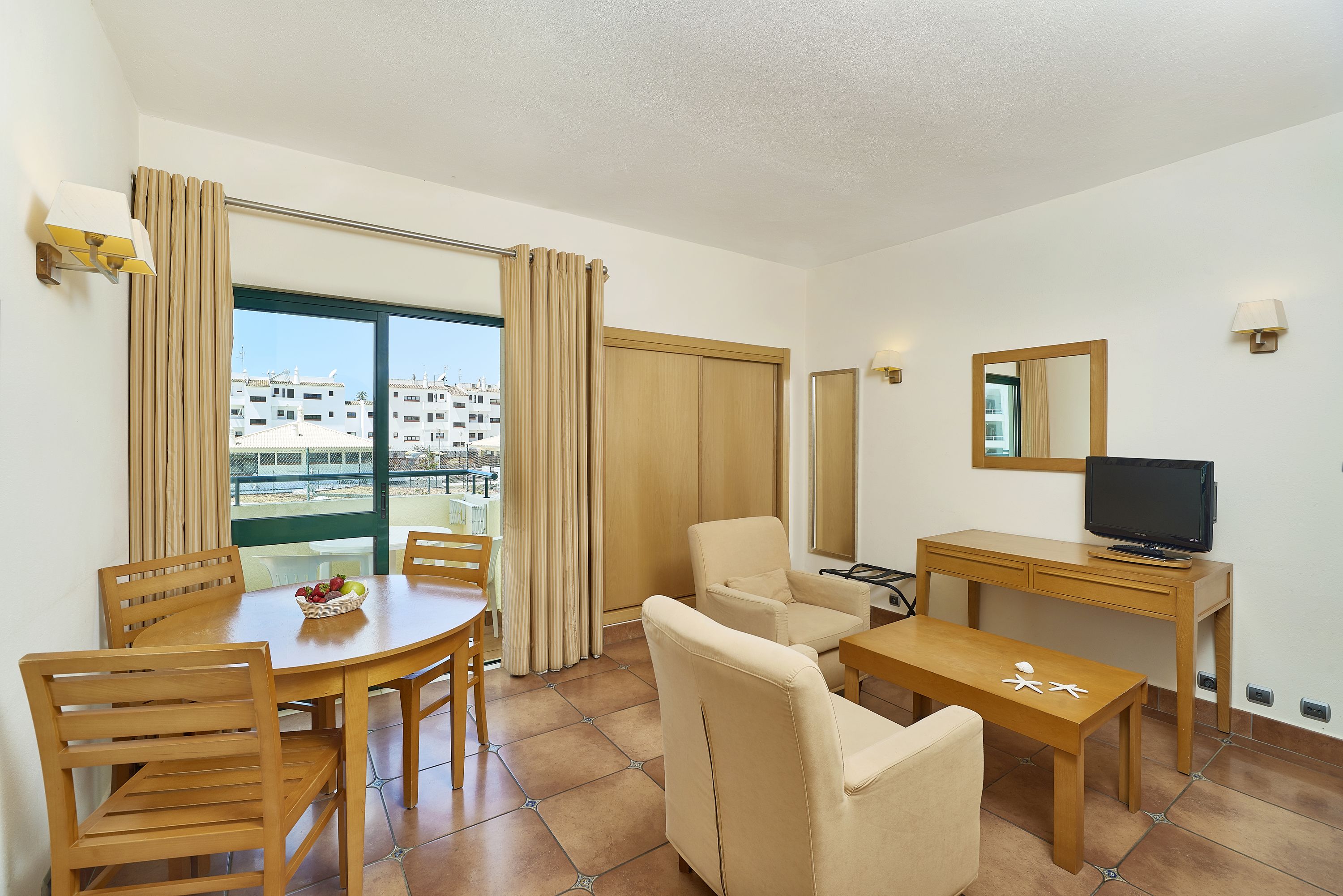 Quarto de hotel com mesa de jantar, duas cadeiras, sofá, televisão e escrivaninha.