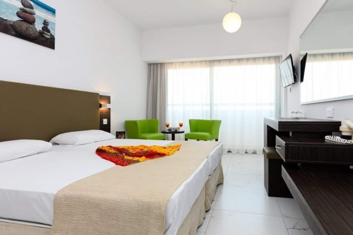 Quarto de hotel com duas camas, uma escrivaninha, uma cadeira, televisão e uma janela grande com cortinas.
