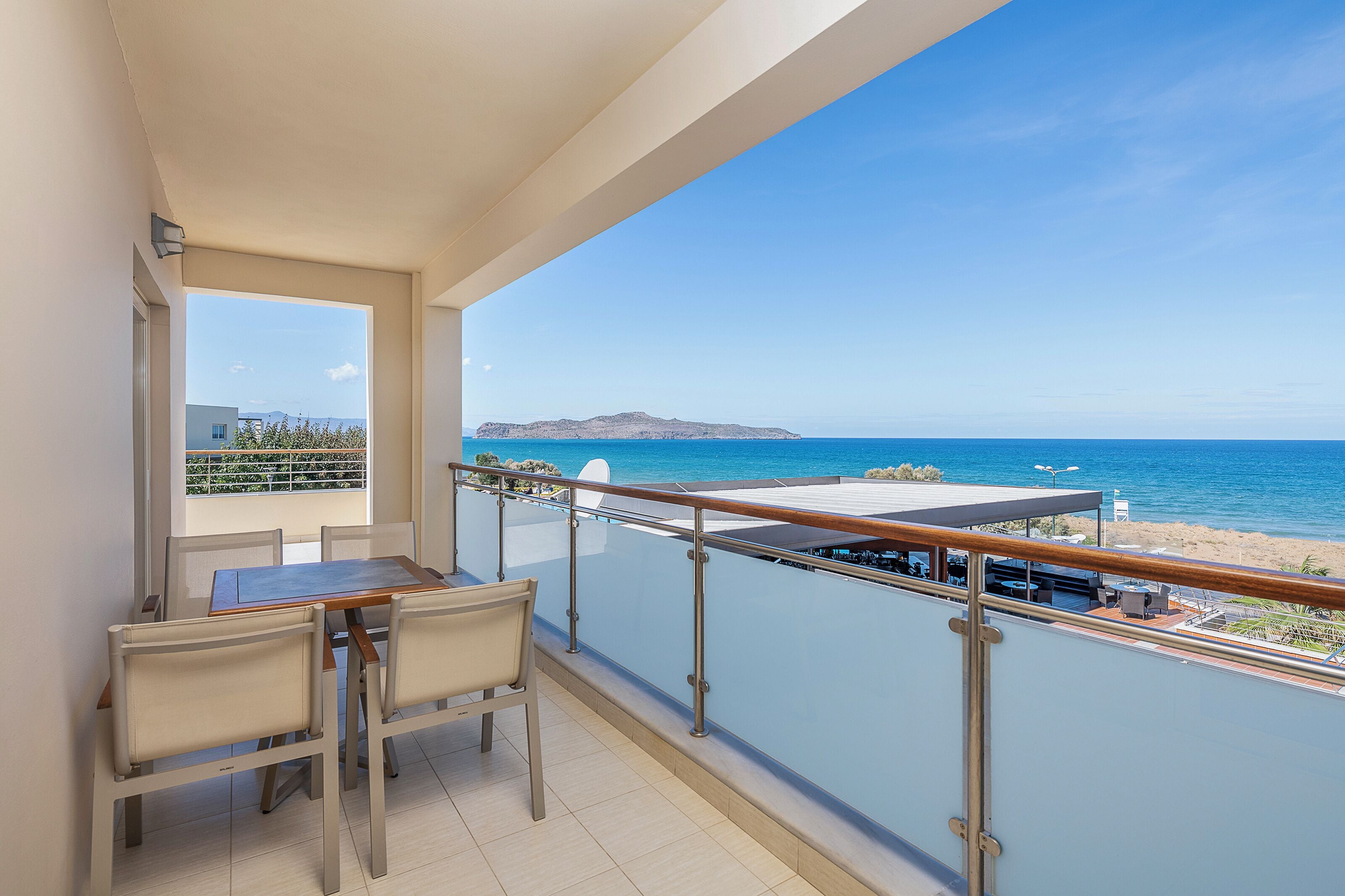 Uma varanda com mesa e cadeiras, com vista para a praia e o oceano.