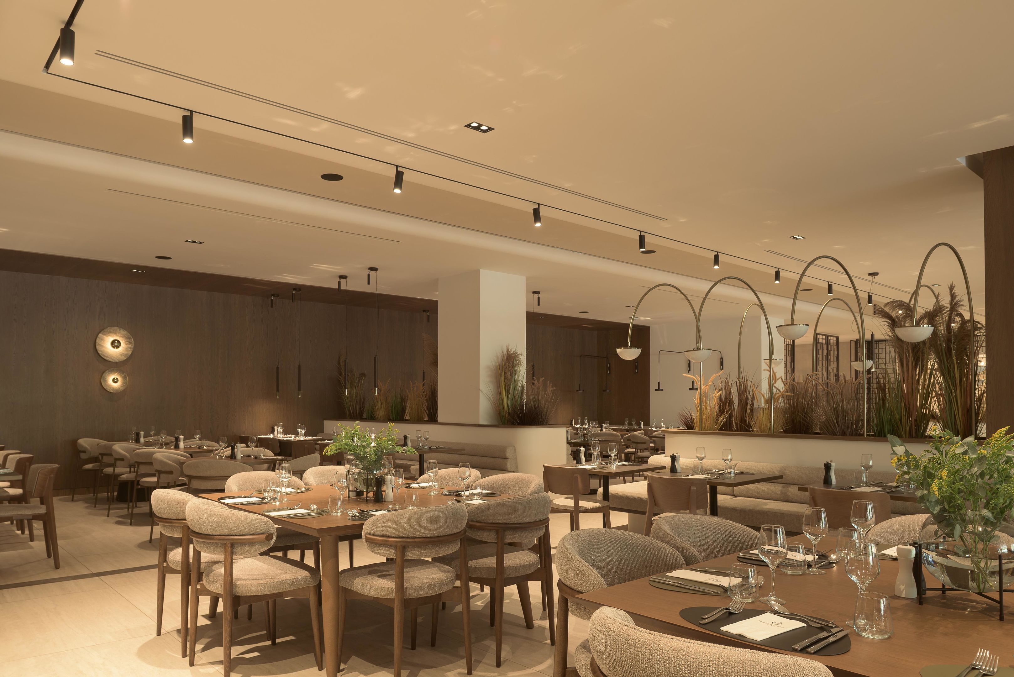 Um restaurante moderno com várias áreas de refeição, incluindo um bar/lounge com banquetas altas e uma sala de jantar principal com mesas e cadeiras redondas.