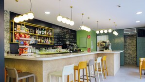 Uma área de bar com balcão, bancos, prateleiras com petiscos e bebidas, e um cardápio em lousa.