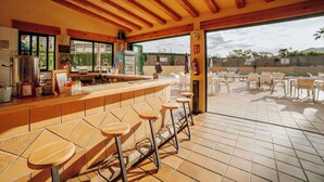 Um café ao ar livre com banquetas de madeira, piso ladrilhado e vista da região.