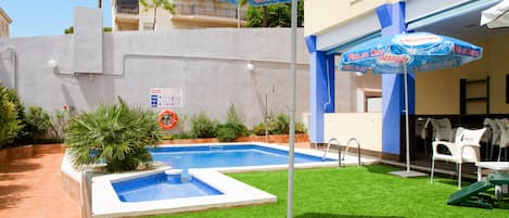 Piscina com grama sintética, um tobogã e guarda-sóis com publicidade de uma marca de água.