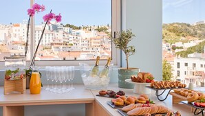 Disposição de café da manhã com champanhe, doces e vista para a cidade.